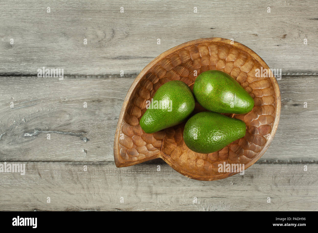Table top view, three whole avocados in wooden carved bowl placed on ...