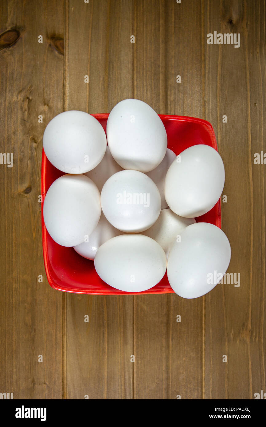 A group of eggs inside a deep red bowl waiting for the chef to use them ...
