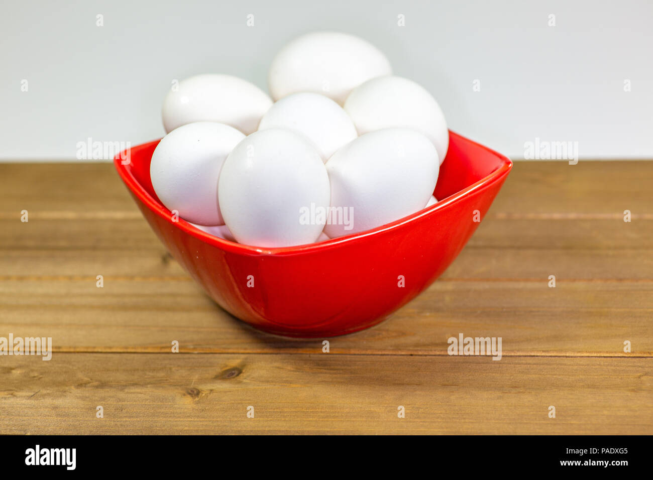 A group of eggs inside a deep red bowl waiting for the chef to use them ...