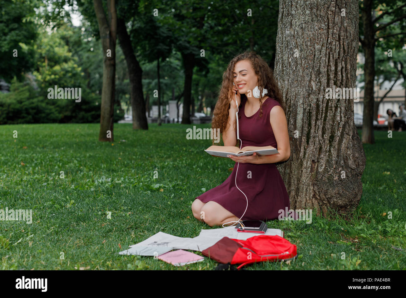 girl student holding book and sitting under tree Stock Photo - Alamy