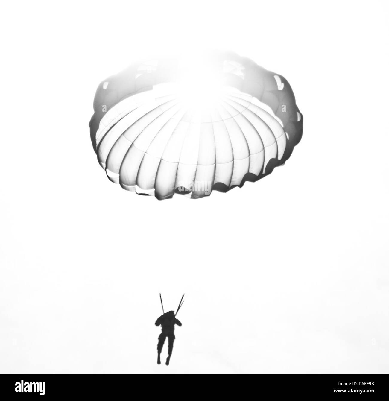A U.S. Army Reserve paratrooper descends in front of the sun during a ...