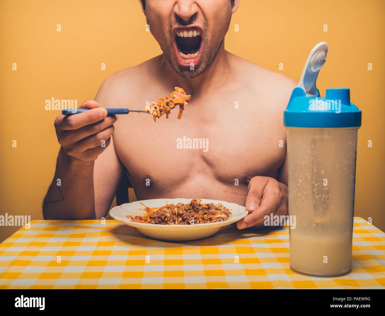 A young fitness man against yellow backdrop is eating mince and protein ...