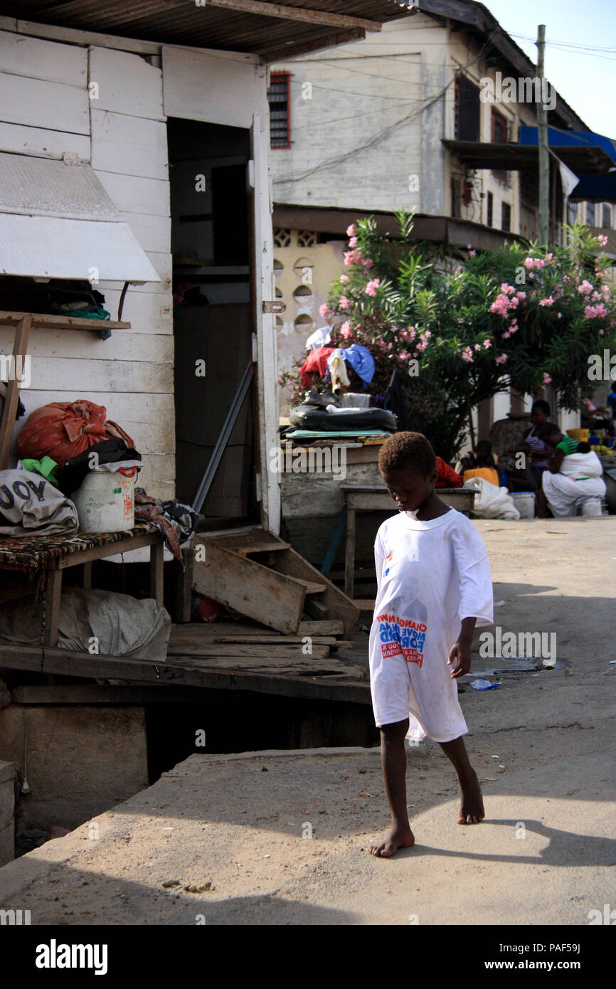 Boy walks along the street in the slum of Cape Coast, passing garbage ...
