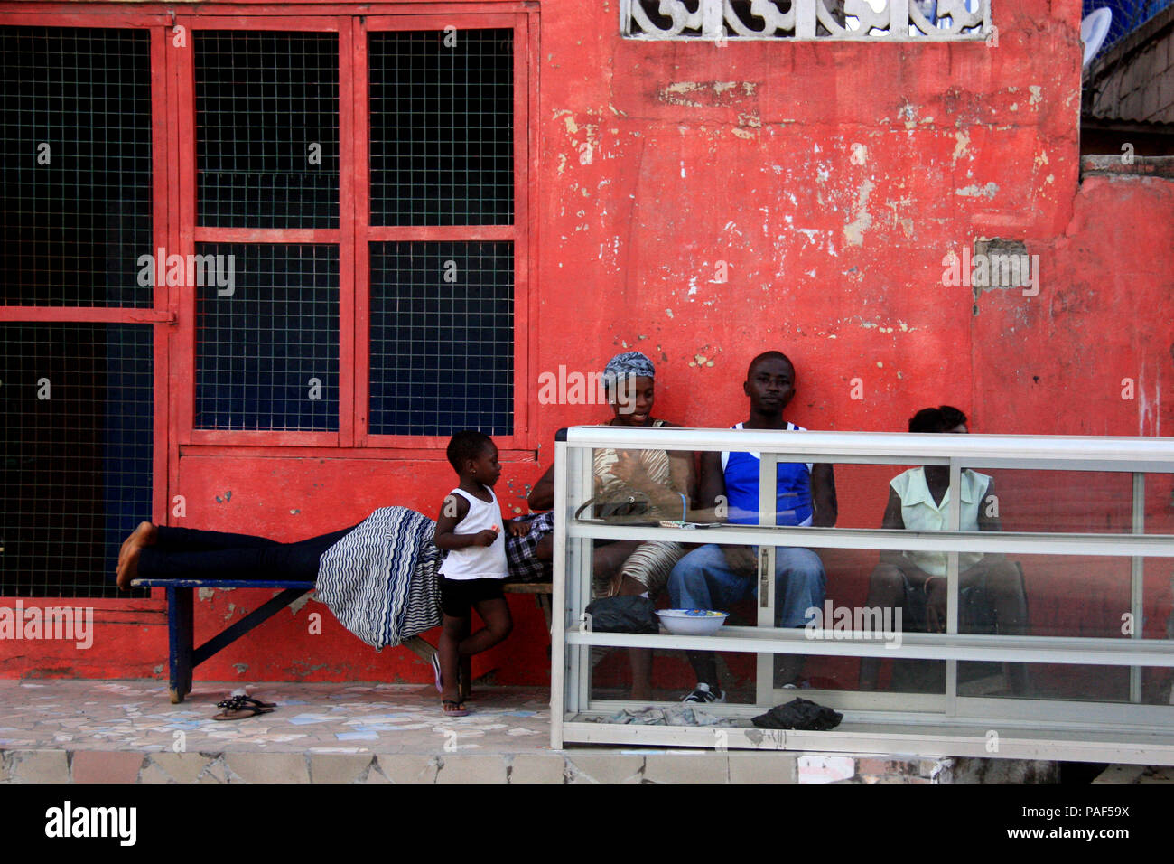 African family sitting on a bench in front of their red colored house ...