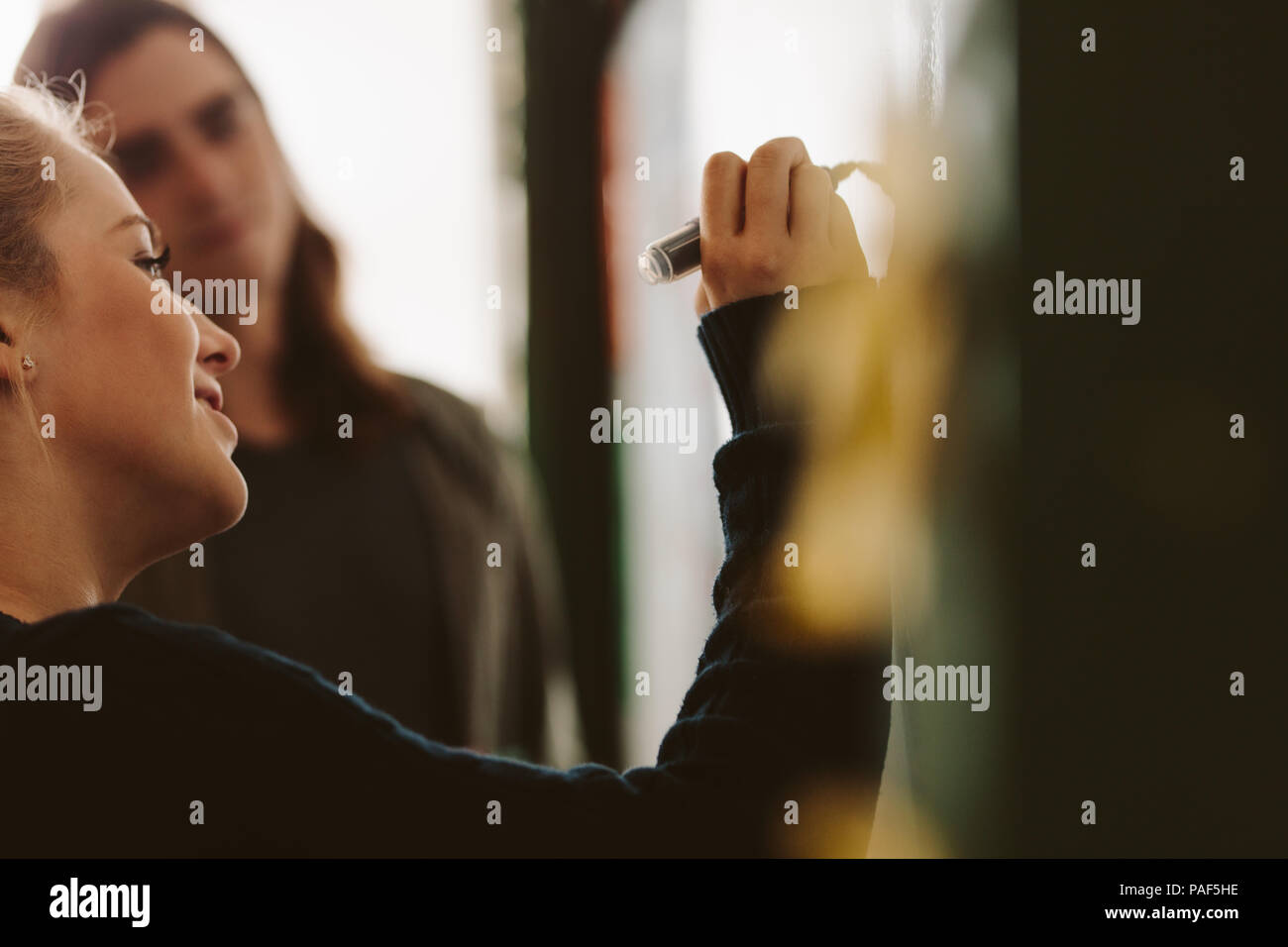 Close up of female student writing an board in classroom with classmate ...