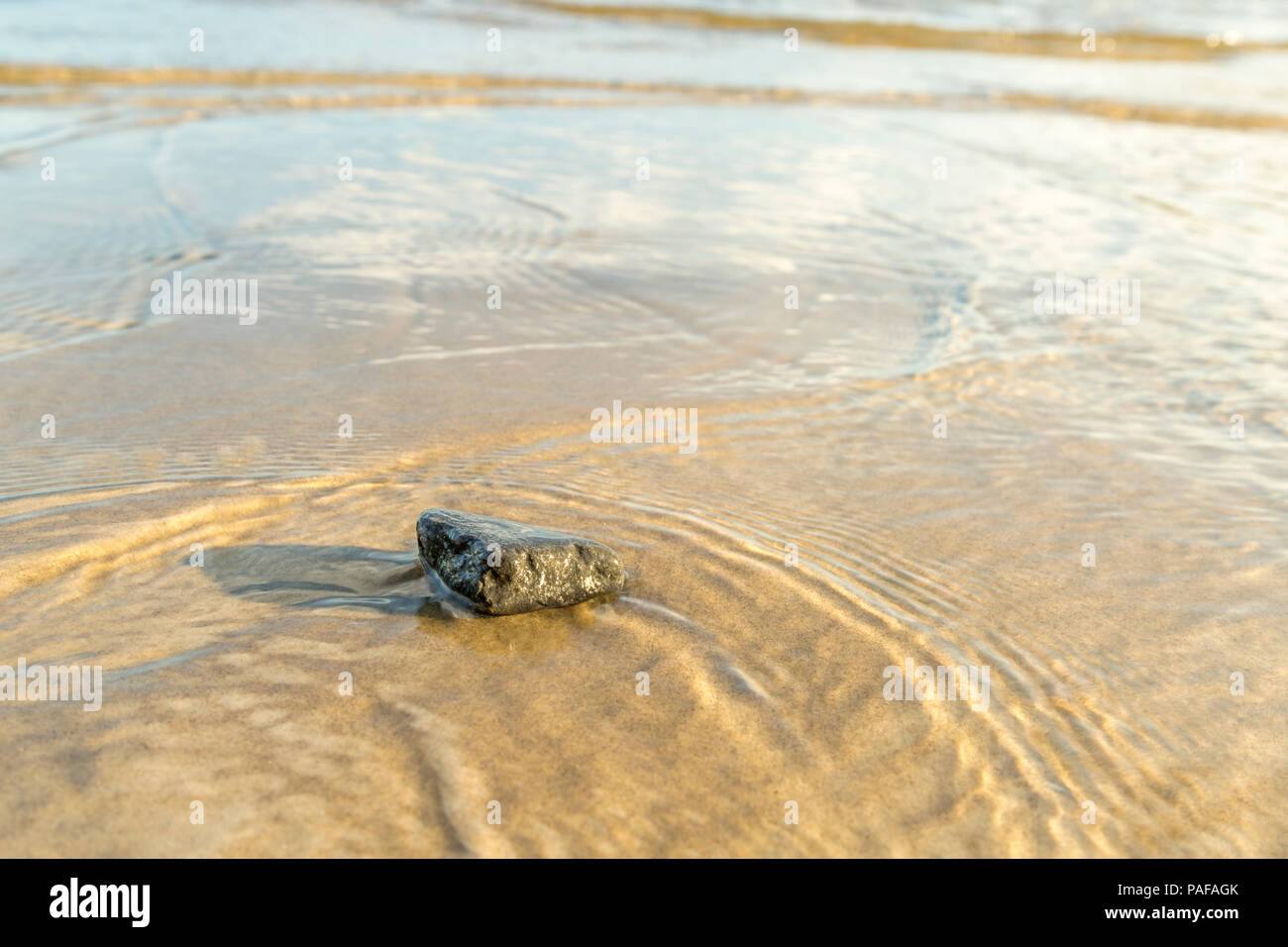 Stone in Sand with Water Ripples close up Stock Photo - Alamy