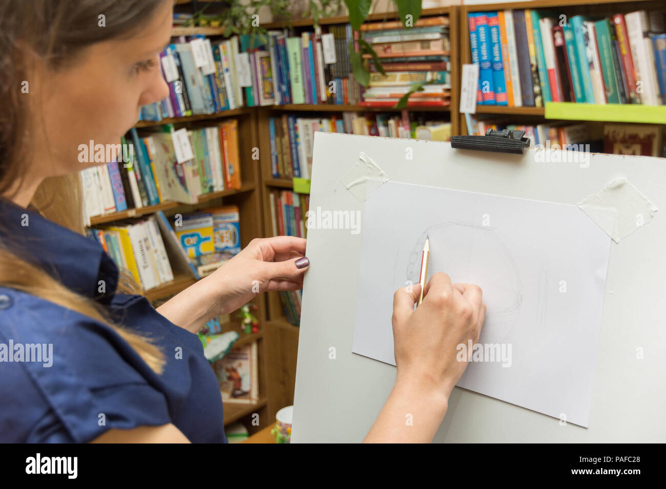 The girl draws on the easel in the library Stock Photo - Alamy