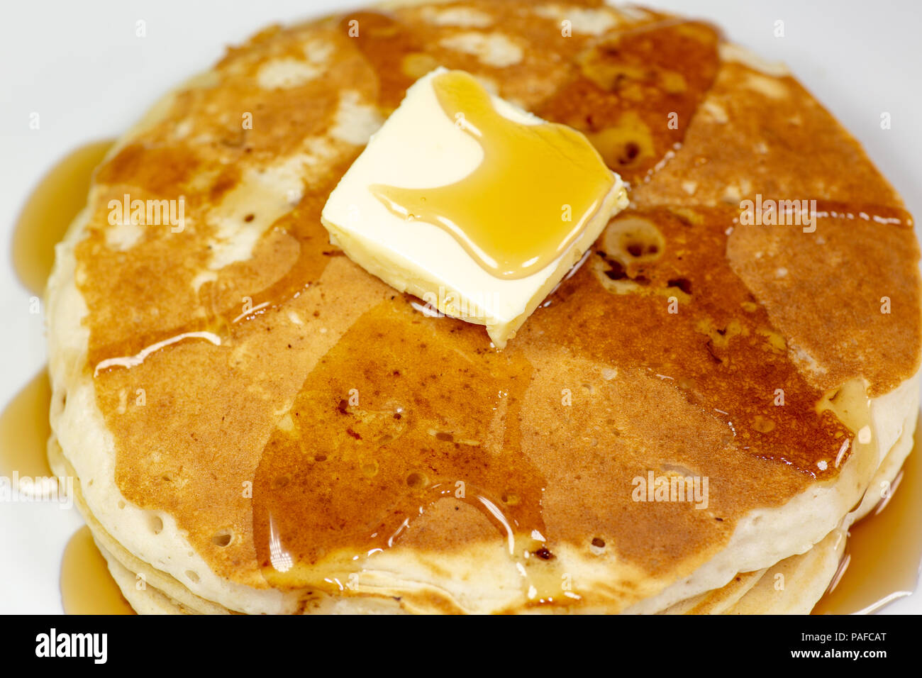 Pancake with a square of butter and syrup on a kitchen table waiting to ...