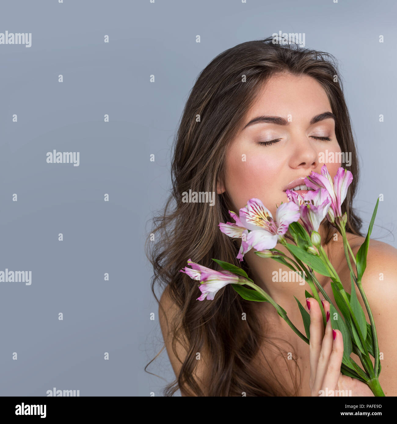 Beautiful girl smelling pink flowers, gray background with copy space ...