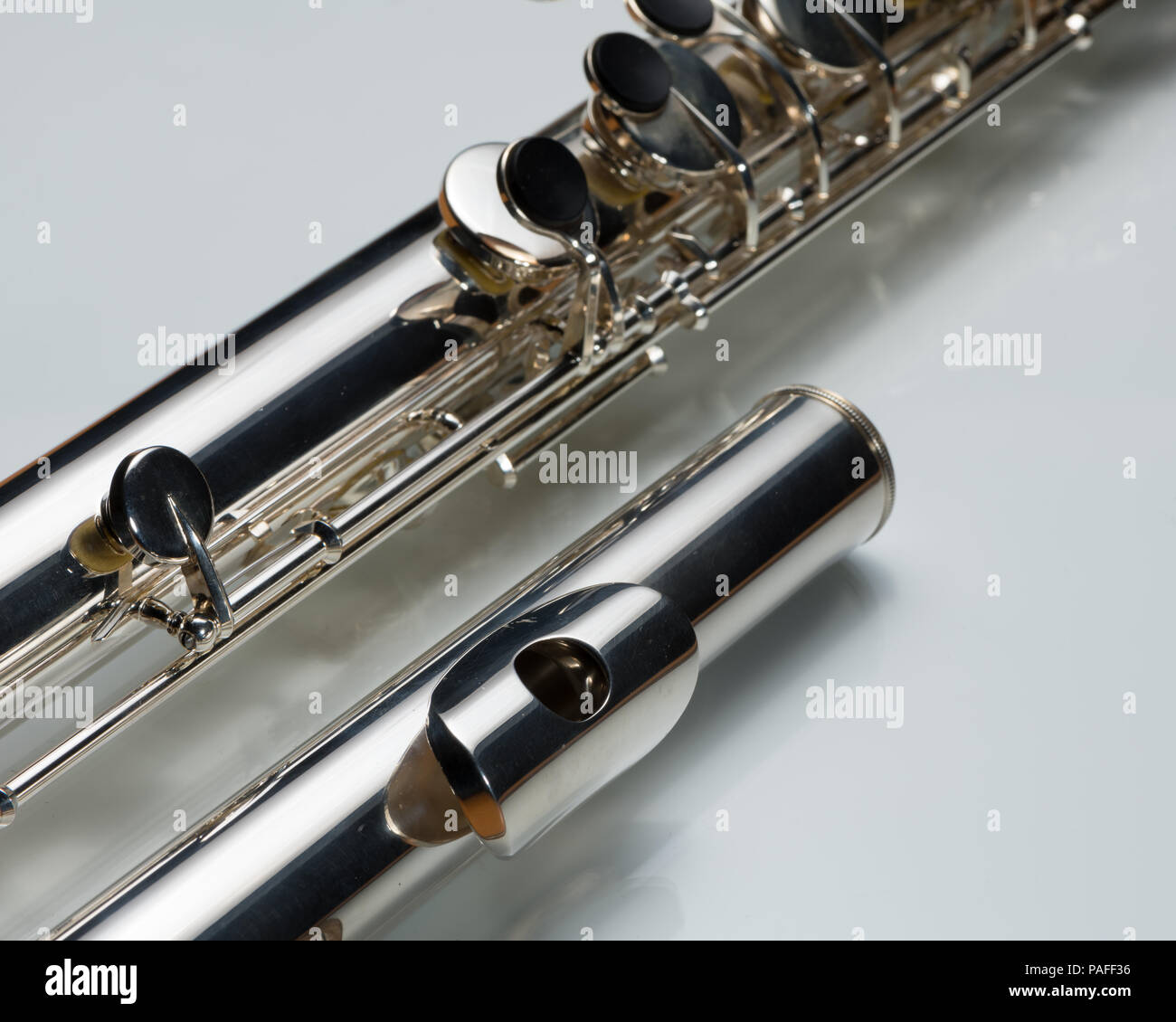 Details of a silver bass flute lying on a white reflective surface ...