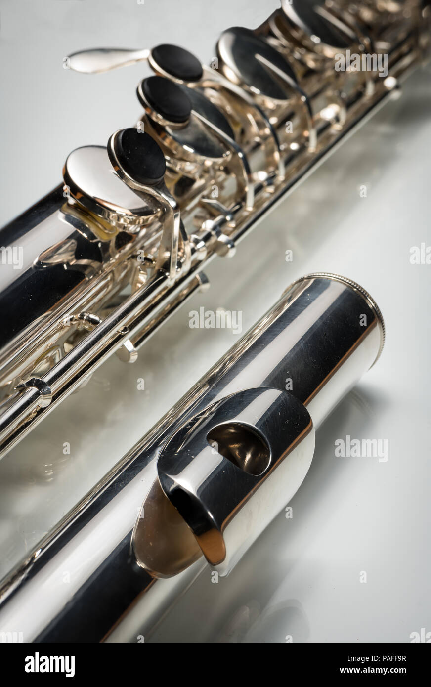 Details of a silver bass flute lying on a white reflective surface ...