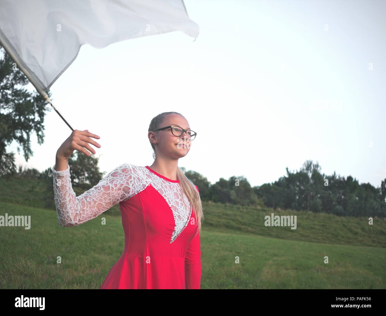 Bespectacled Blonde Teen Majorette Girl with White Flag Outdoors in Red ...