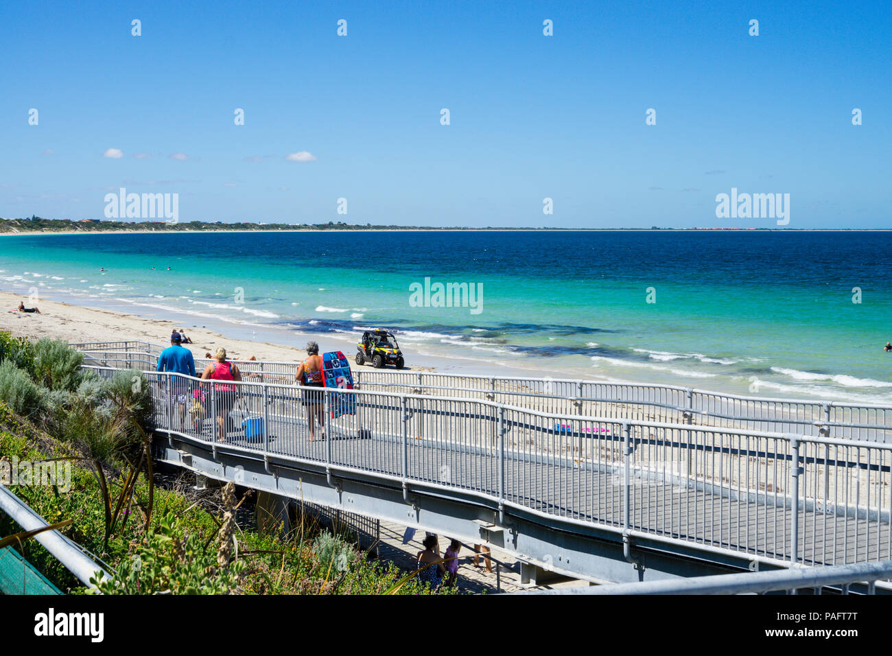 People walking down ramp to sandy white beach with clear blue sea ...