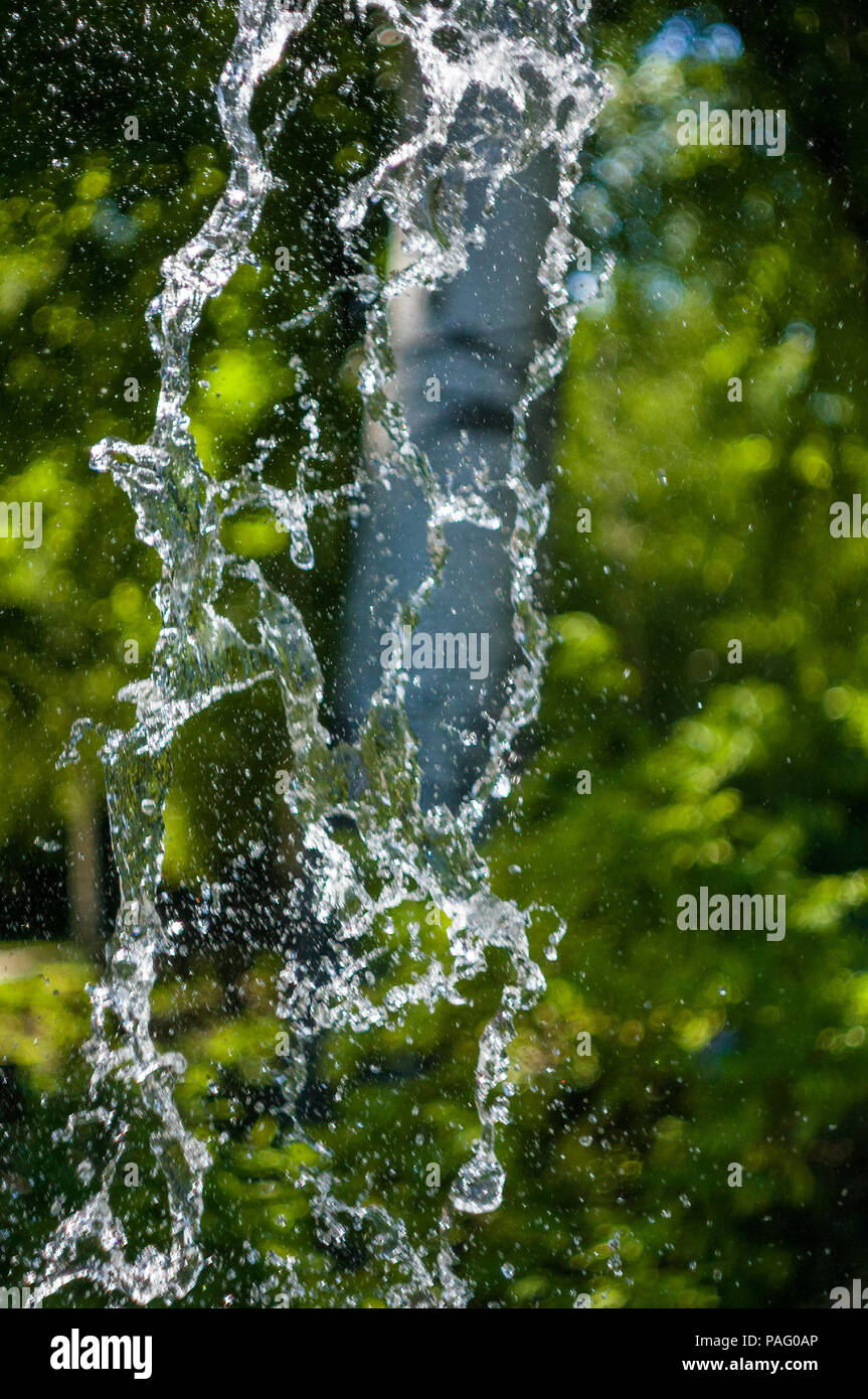 transparent falling water vertical flows against a blue sky and green ...