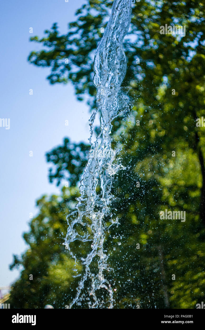 transparent falling water vertical flows against a blue sky and green ...