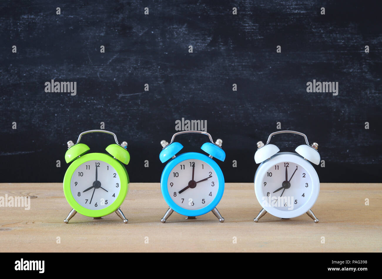 A collection of colorful alarm clocks over wooden desk in front of ...