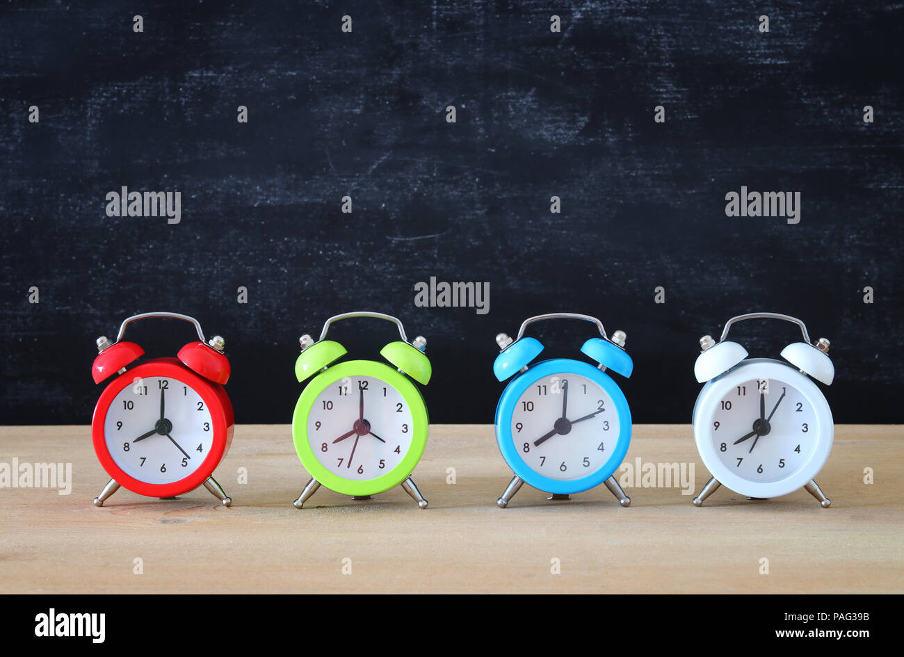 A collection of colorful alarm clocks over wooden desk in front of ...