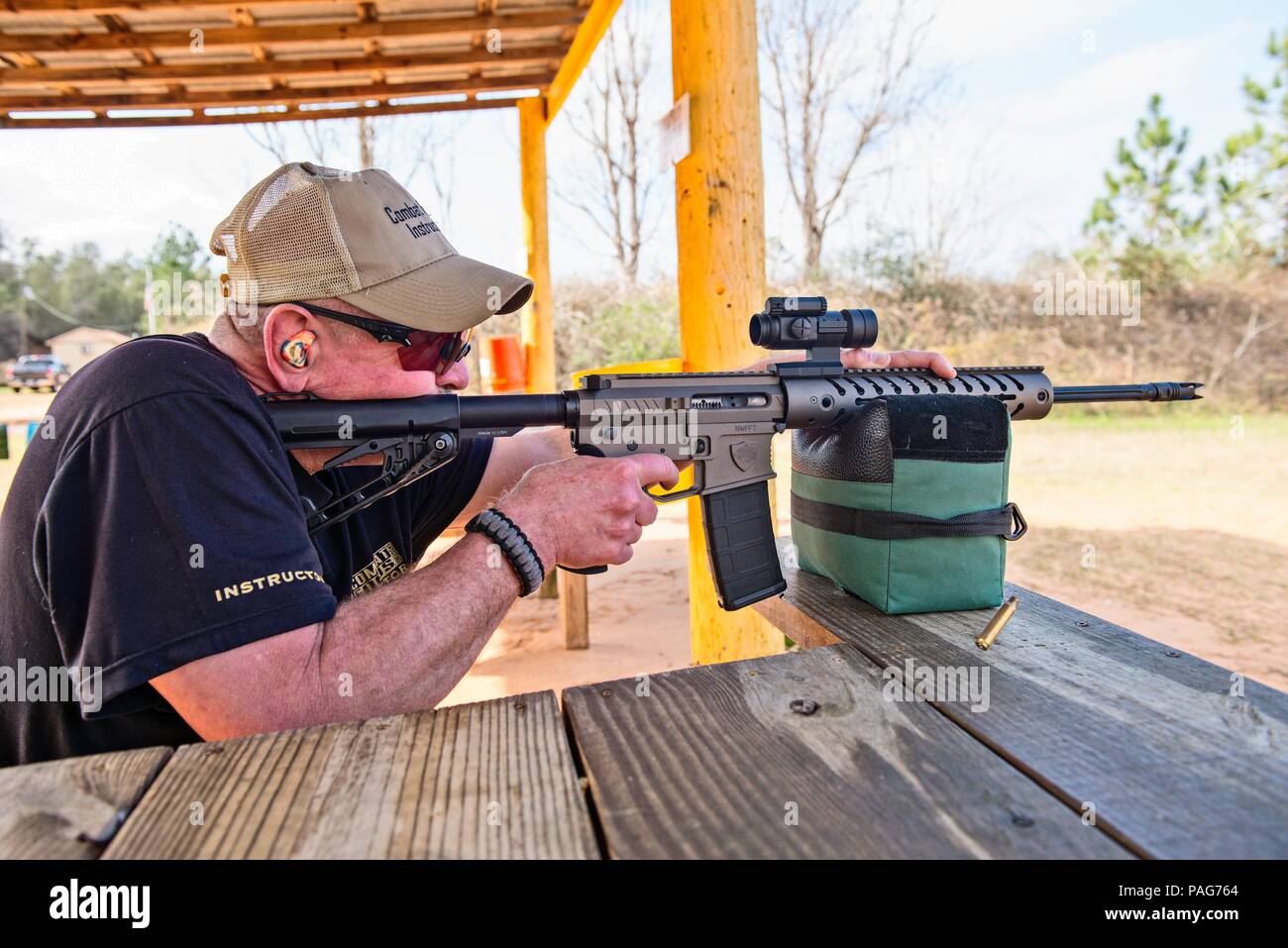 A sits on a bench at a table while looking through the scope of an AR ...