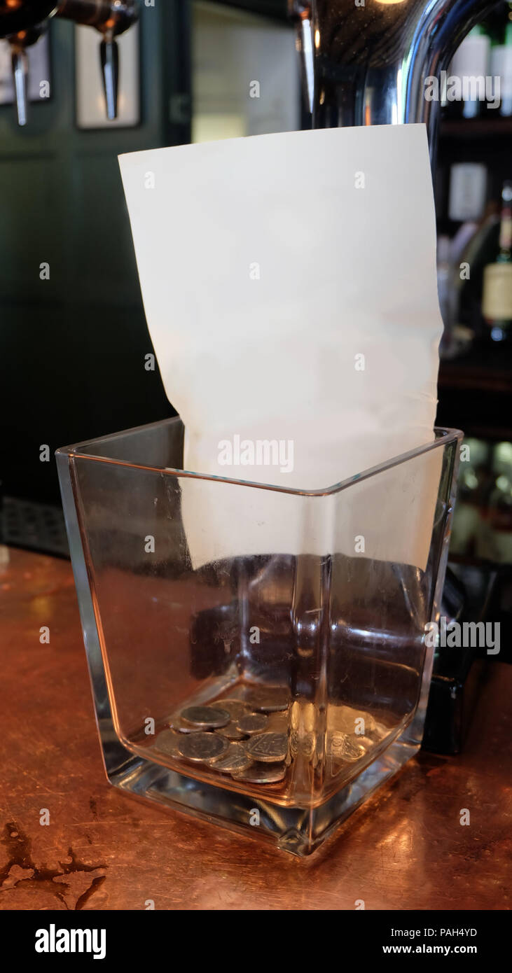Clear glass tip box on a bar counter, with some coins and a blank piece ...
