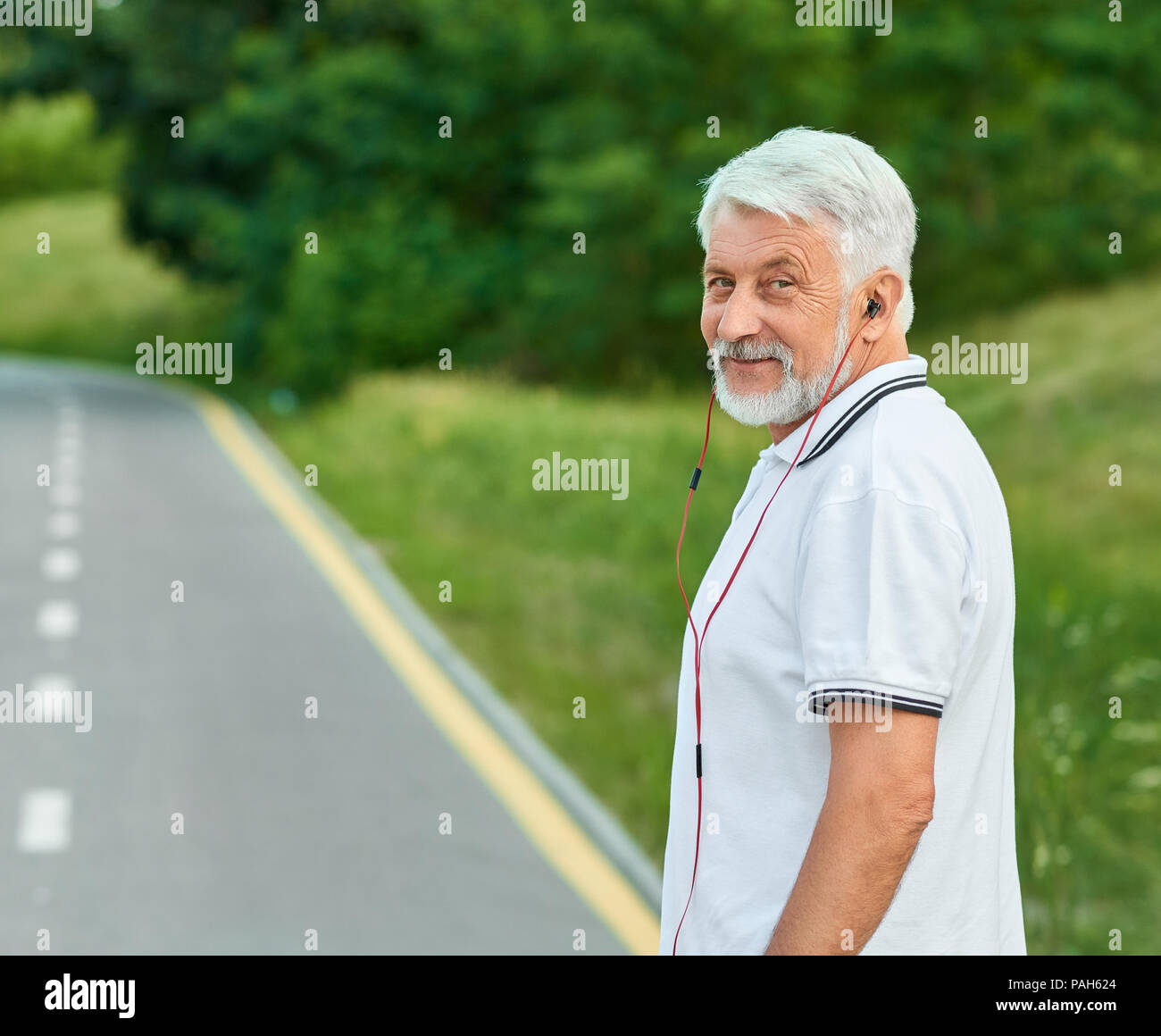 Smiling old man standing on city's racetrack looking at camera. Wearing ...