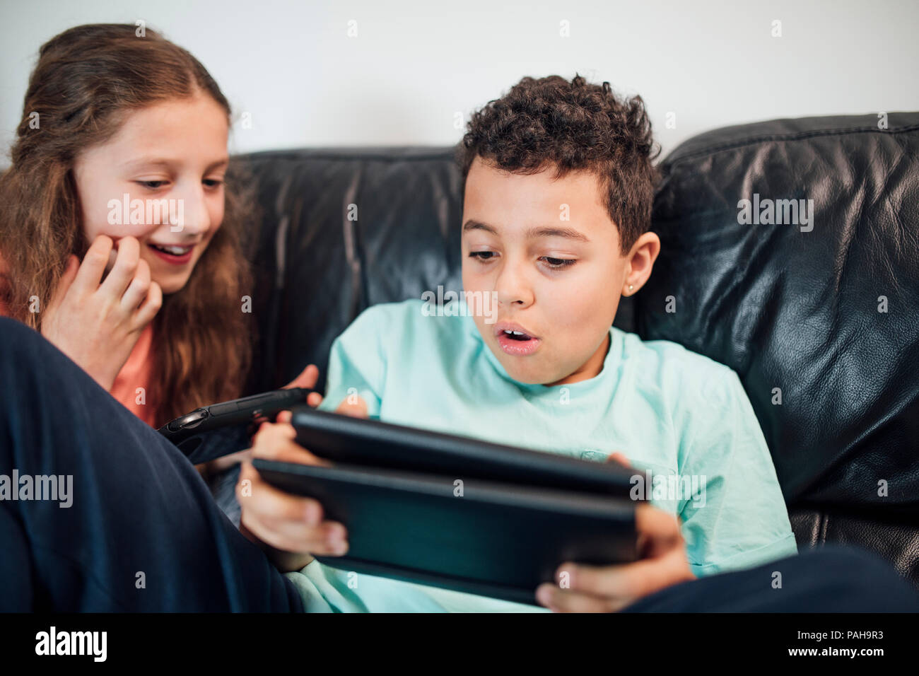 Little boy and his sister are playing on handheld game consoles at home ...