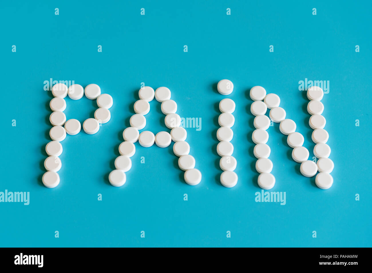 the inscription of pain is laid out with white pills on a blue ...