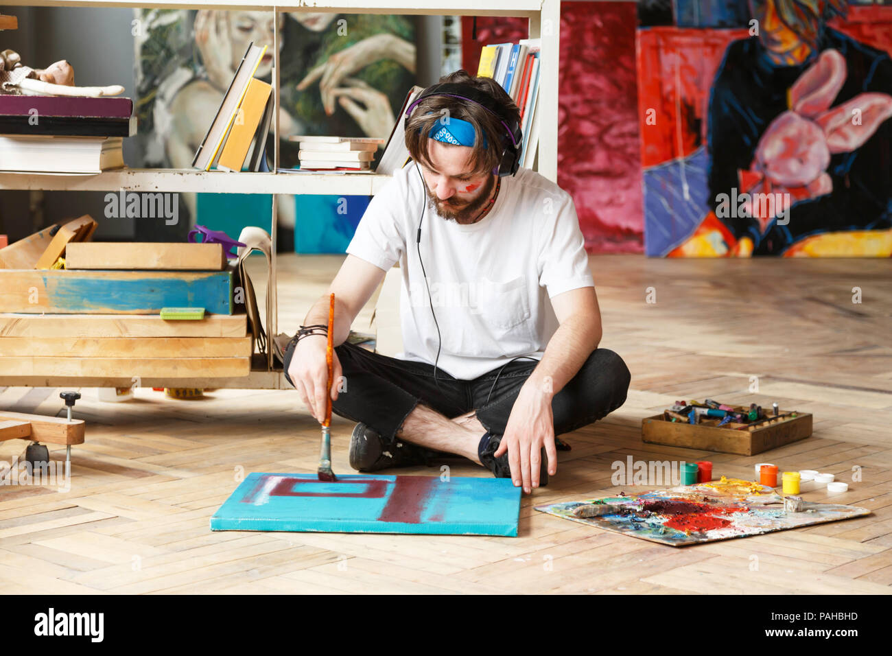 Creative dark-haired bearded hipster male artist in headphones and blue ...