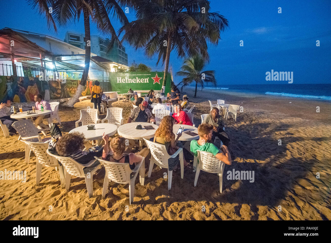 Groups of people are seated at tables along the beach at a restaurant ...