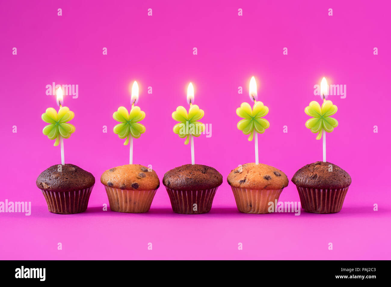 Five Cupcakes with burning cloverleaf candles over a pink background ...