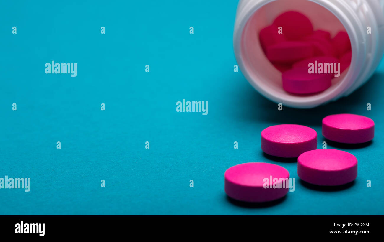 Medication bottle and bright pink pills spilled on dark blue coloured ...