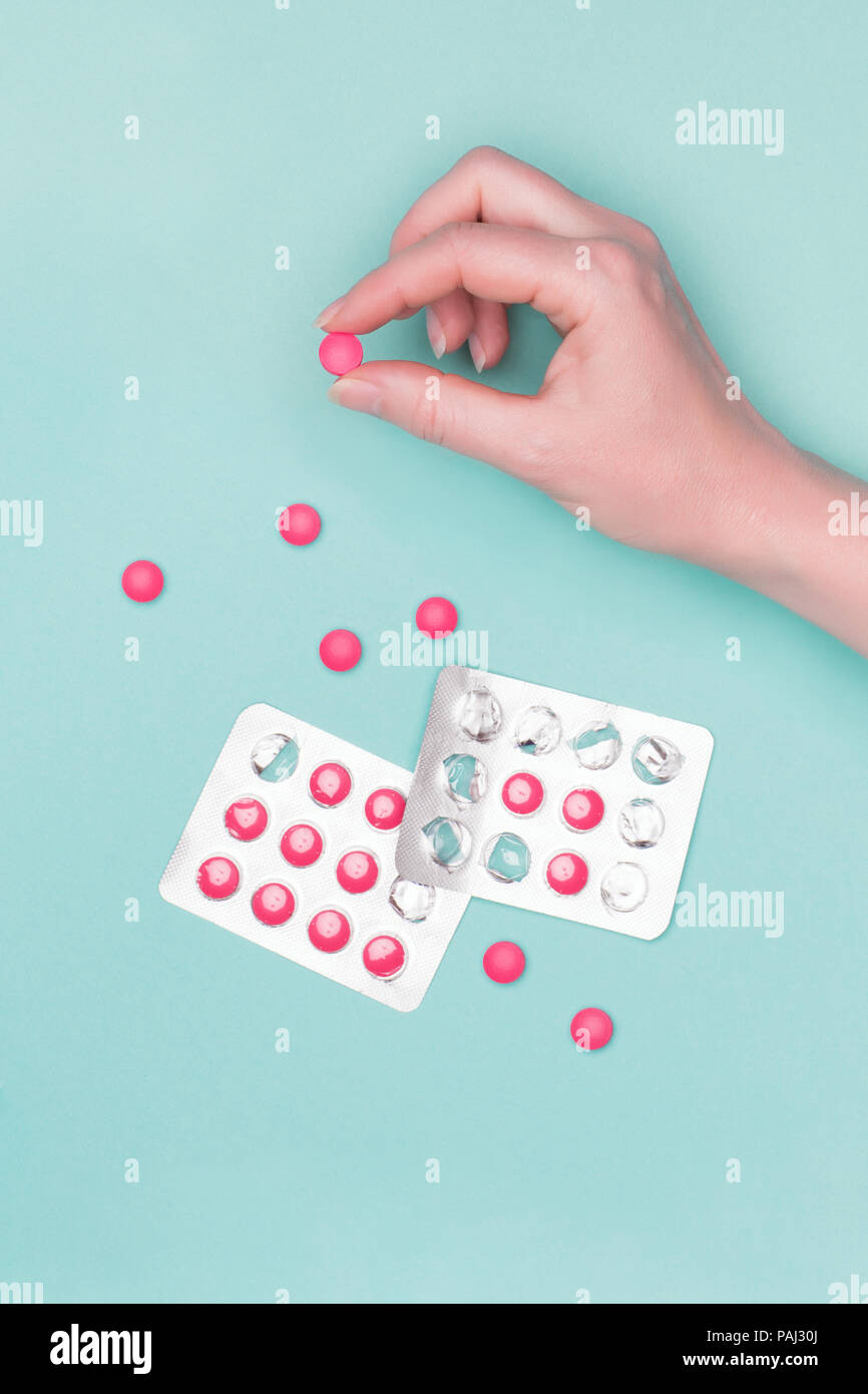 Top view of female hand holding pink prescription pill next to blister ...