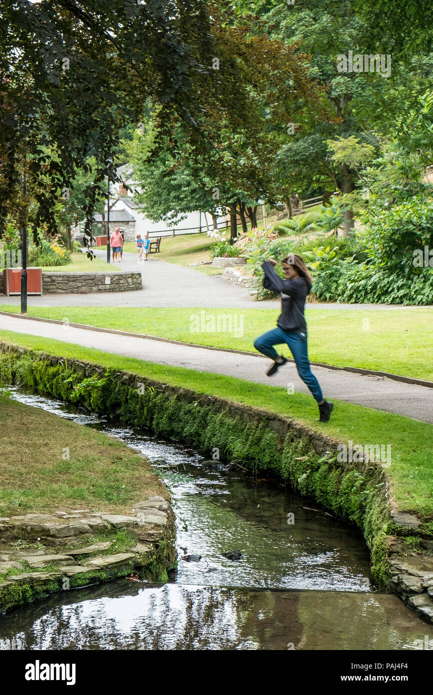 A teenage girl jumping over a stream in Trenance Garden in Newquay ...