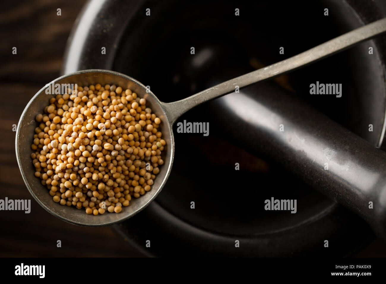 Raw, unprocessed mustard seed kernels in metal scoop on black mortar ...