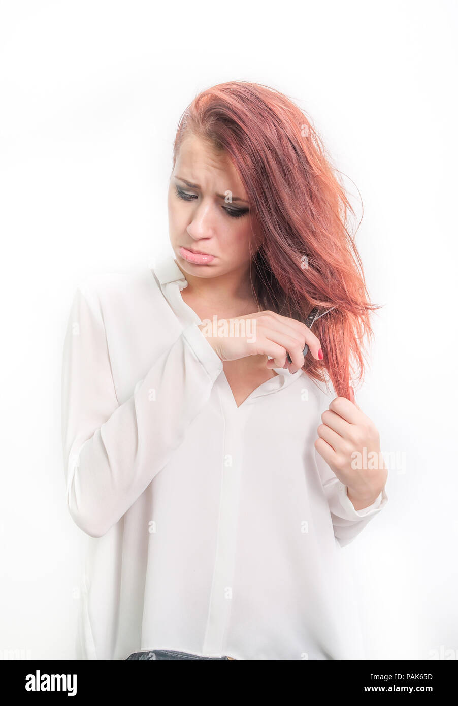 Beautiful redhead young female cutting her hair with a sad expression ...