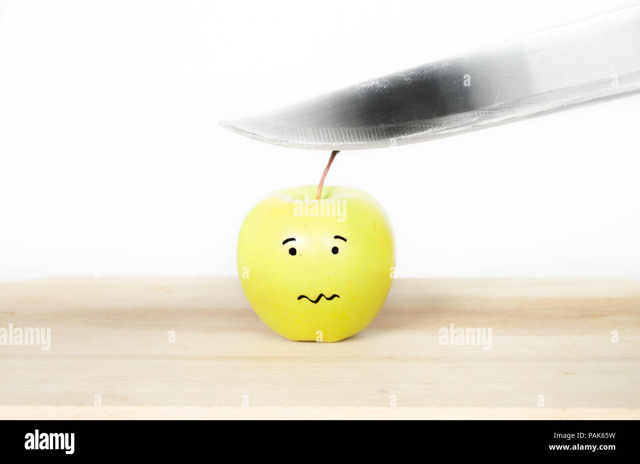 Green yellow apple with a comic face being threatened by a knife blade ...