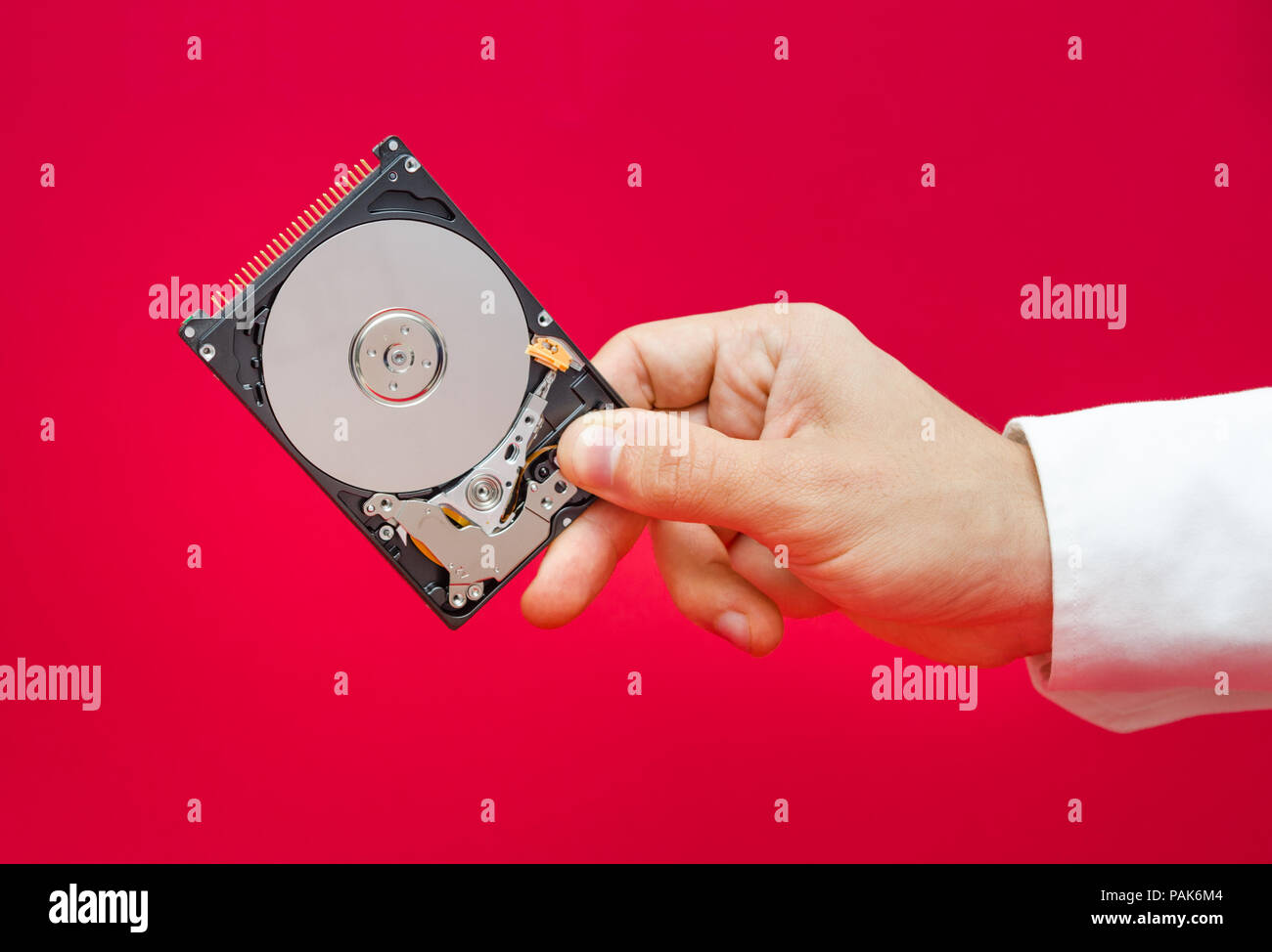 A hard disk being held by a business hand on a red background ...