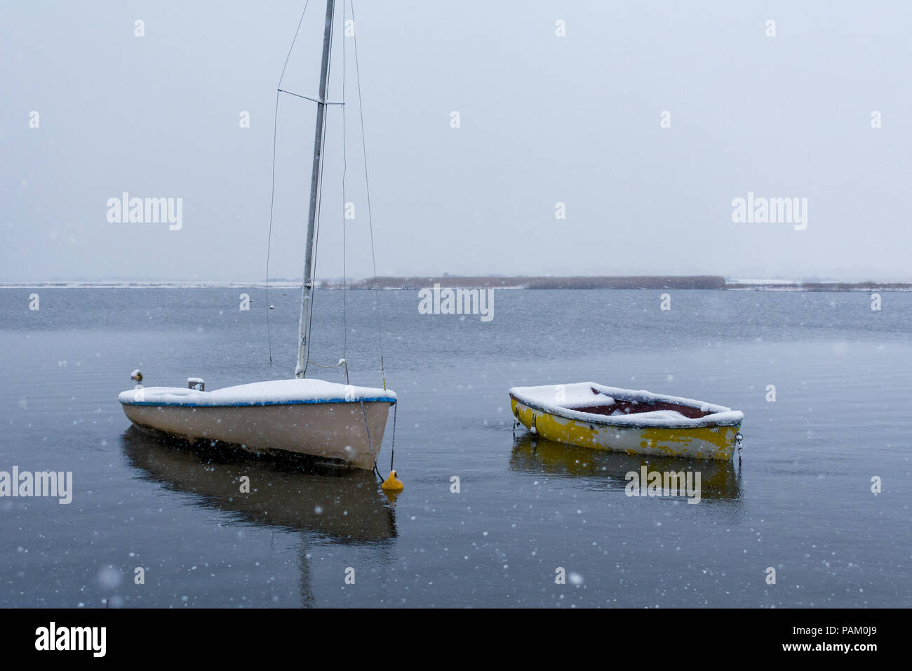 Two snow covered boats floating in a harbour during a winter snow storm ...