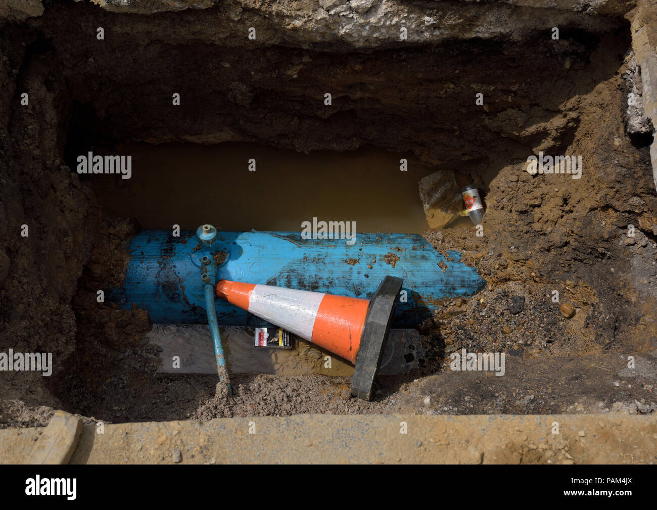 Blue water main pipe leaking into hole under pavement with traffic cone ...