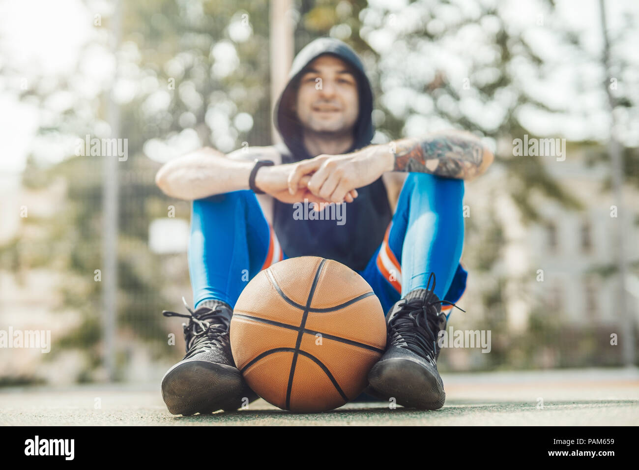 Bald attractive man sitting under basketball hoop and board on the ...