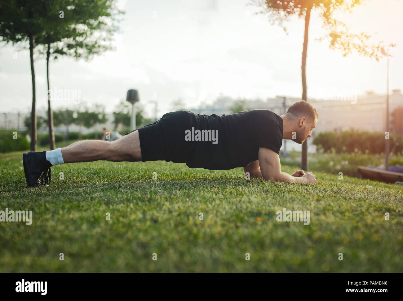 Distant plan of young attractive man exercising plank outdoors. Back ...