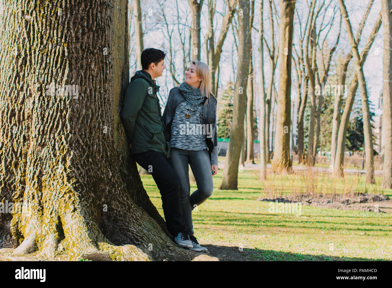 A beautiful loving couple smiling and kissing a large tree in the park ...