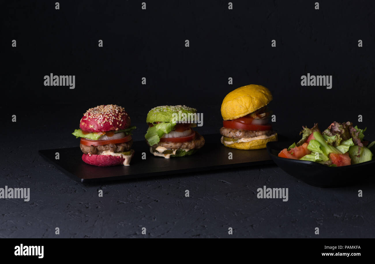 set of variated color cheeseburgers on a flat plate on a black ...