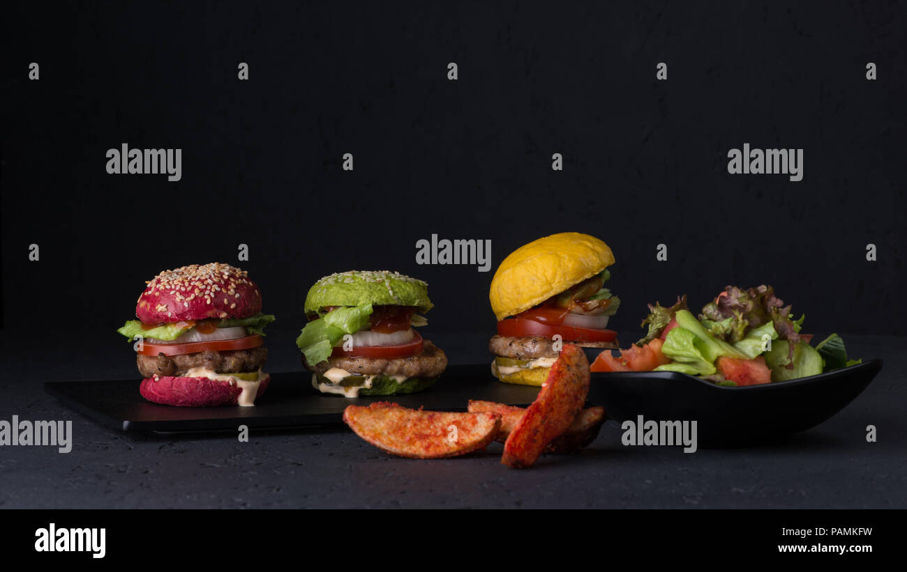 set of variated color cheeseburgers on a flat plate on a black ...