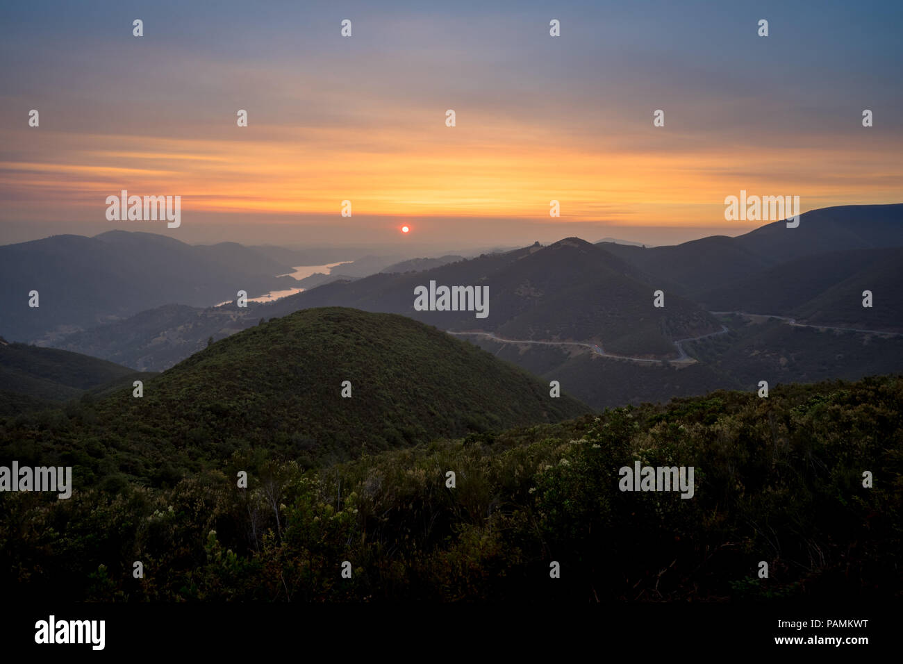 Snaking mountainside road and blood red sun setting in smoky forest ...