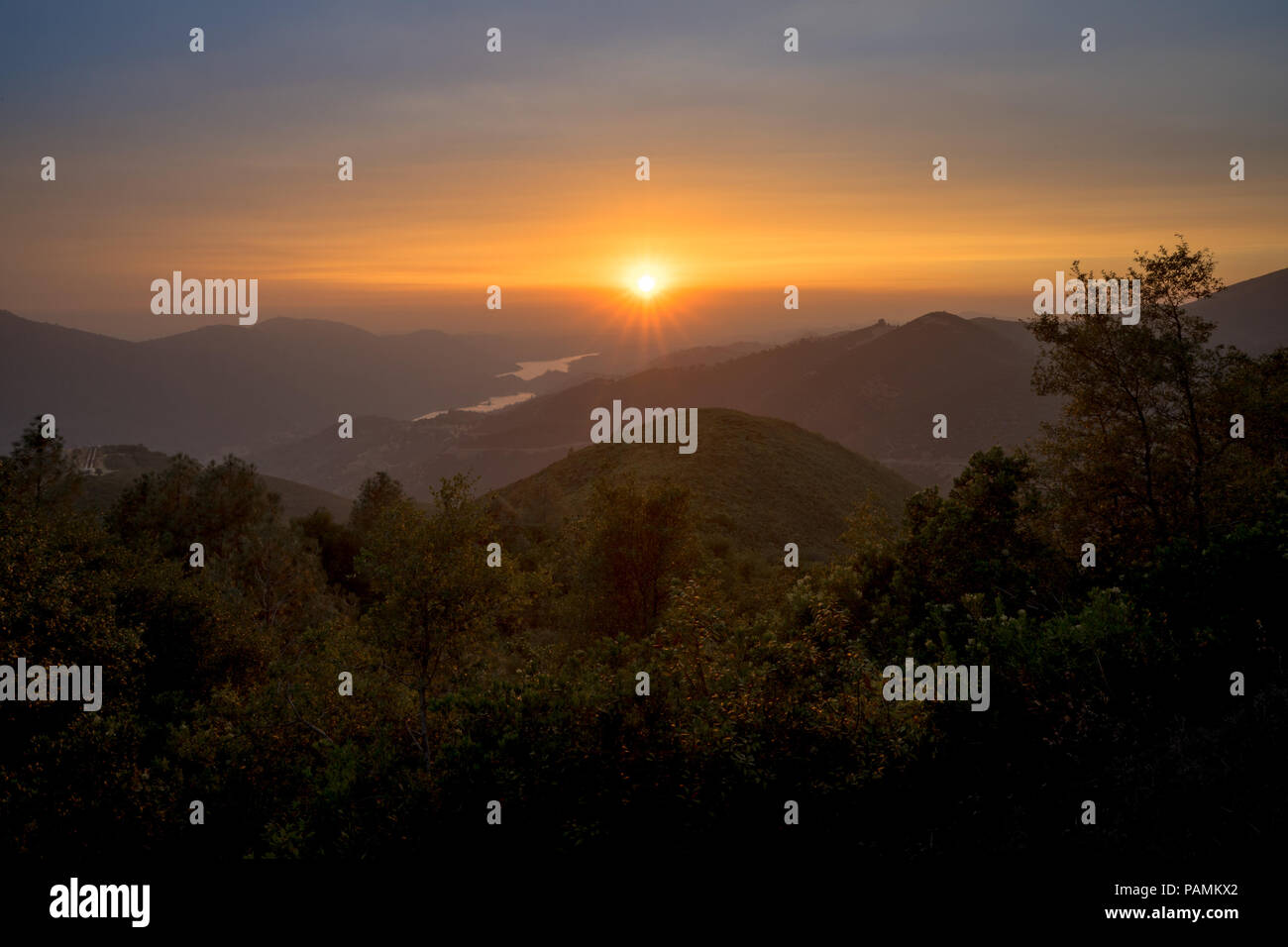 Orange setting sun dipping below a layer of smoky wildfire haze ...
