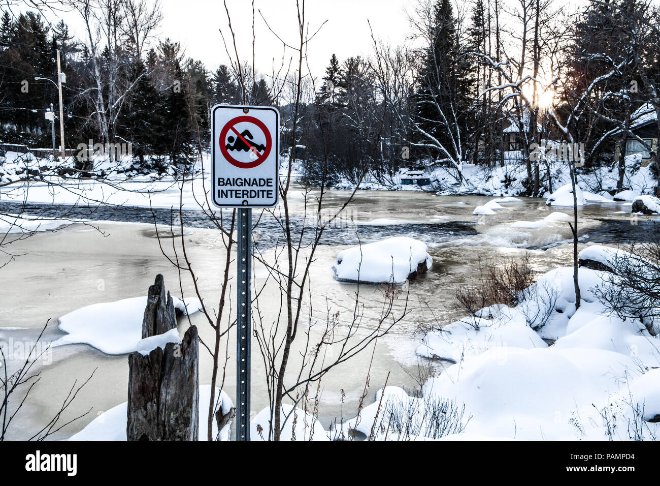 Swimming forbidden sign in front of a partially frozen, fast flowing ...