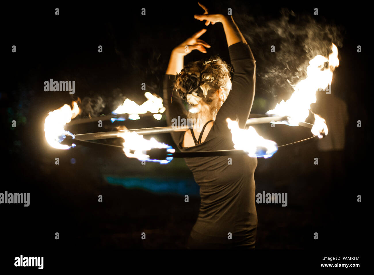 Woman spinning fire at night, in front of an audience, seen from behind ...