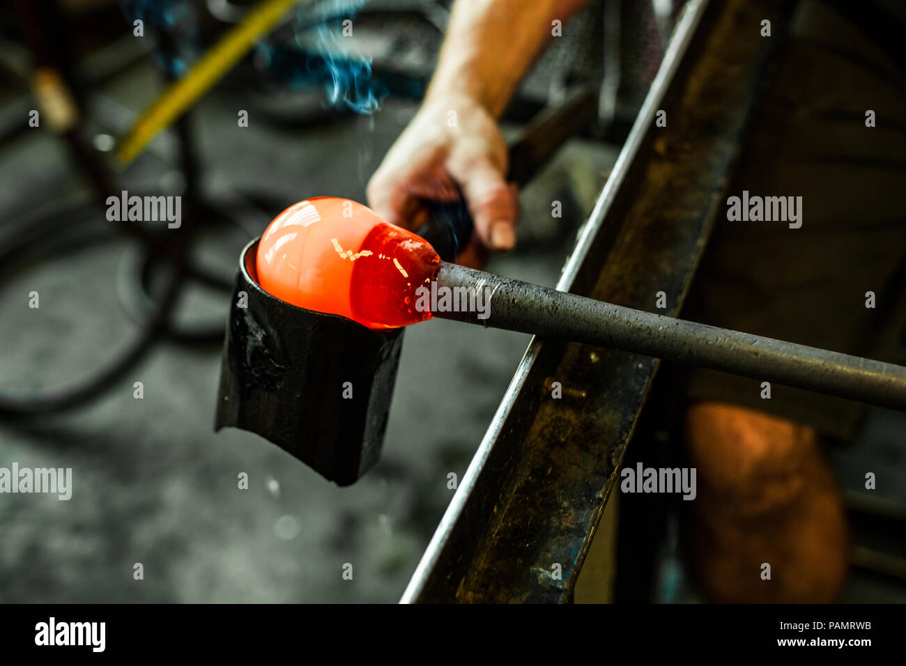 Glass-blower man working with hot orange glass to make a blown glass ...