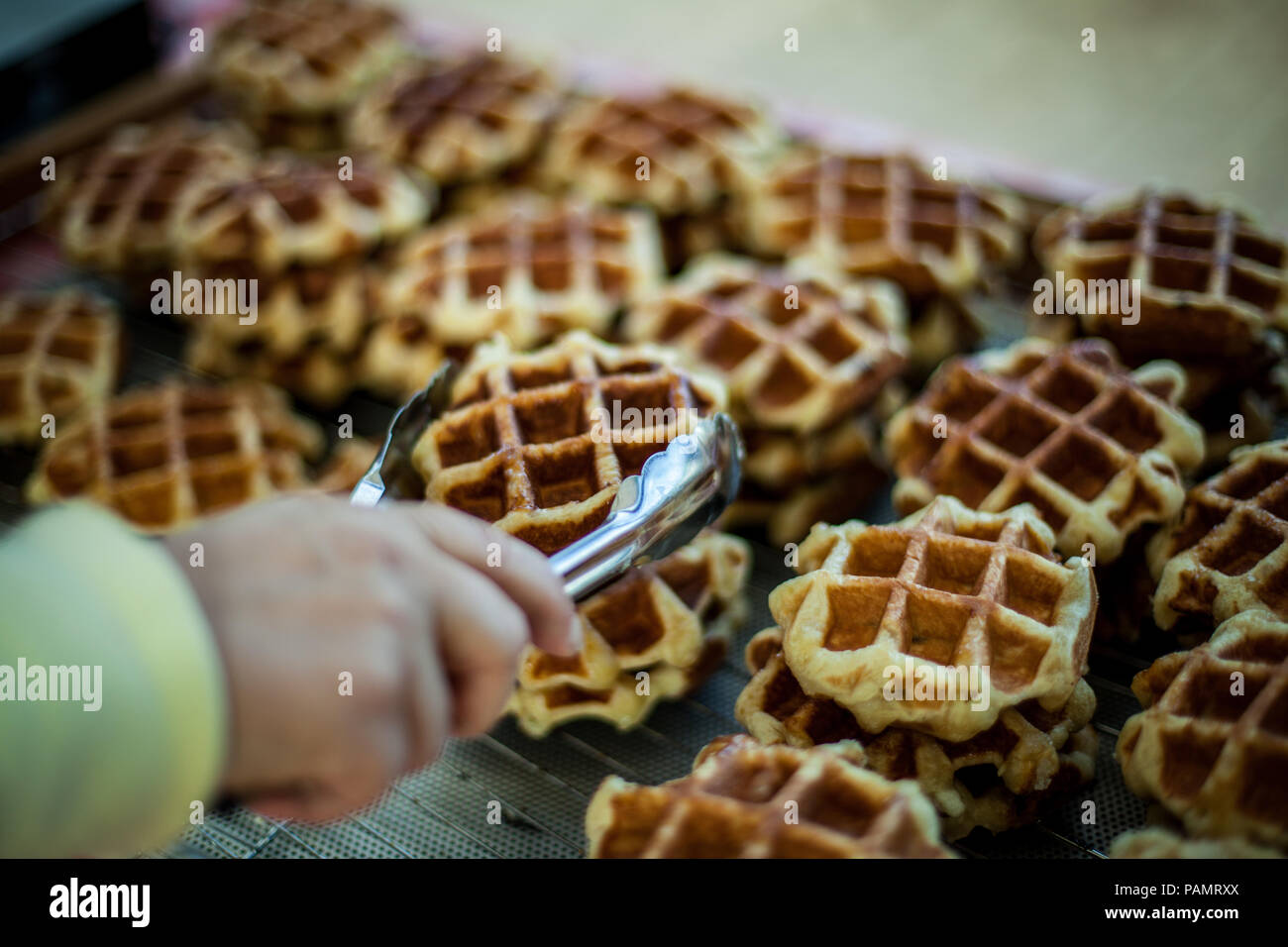 Hand holding a big waffle in kitchen tong, with more waffles in the ...