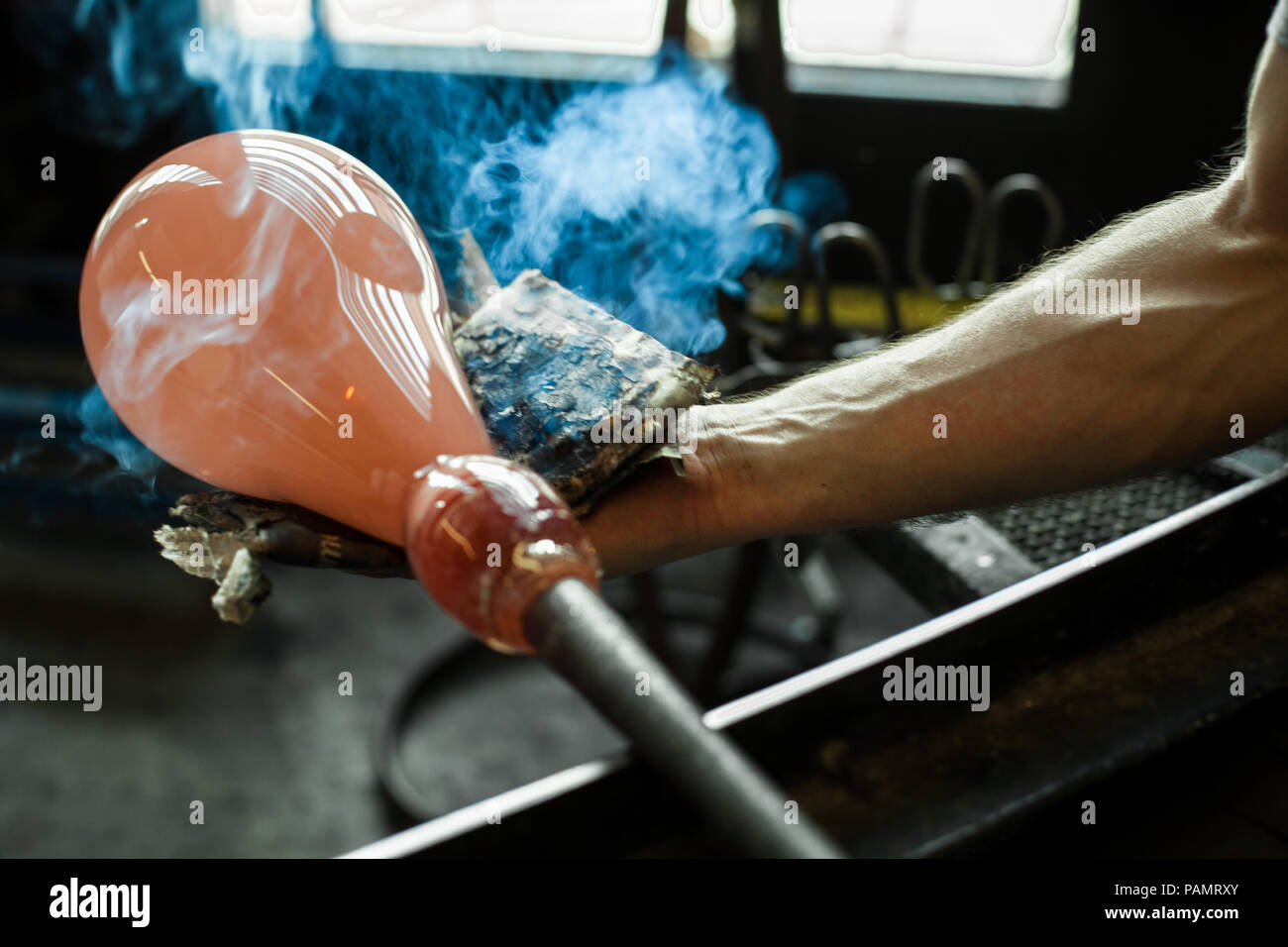 Glass-blower man working with hot ocher glass to make a blown glass ...